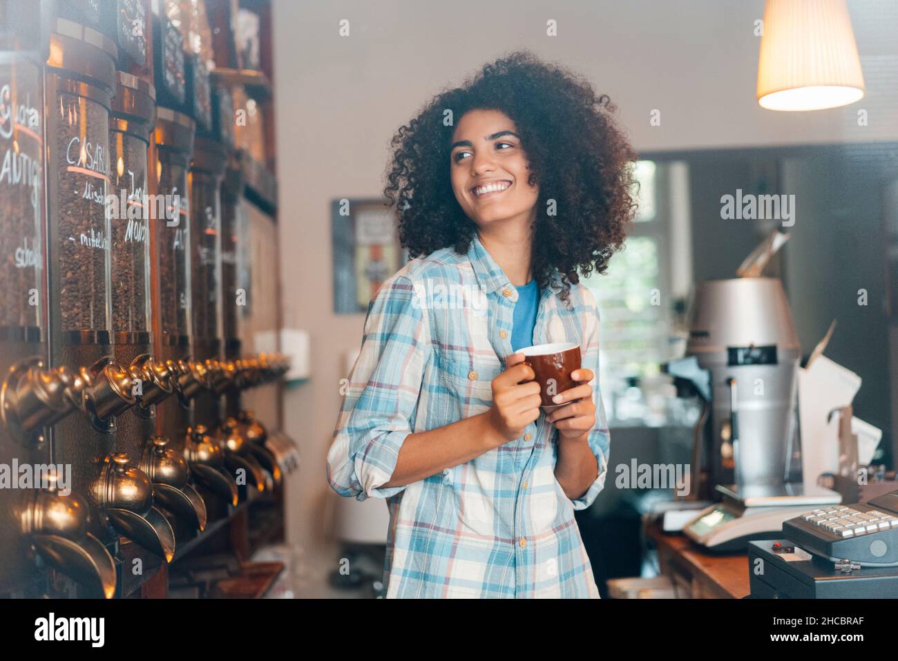 Smiling owner with coffee cup standing in roastery Stock Photo - Alamy