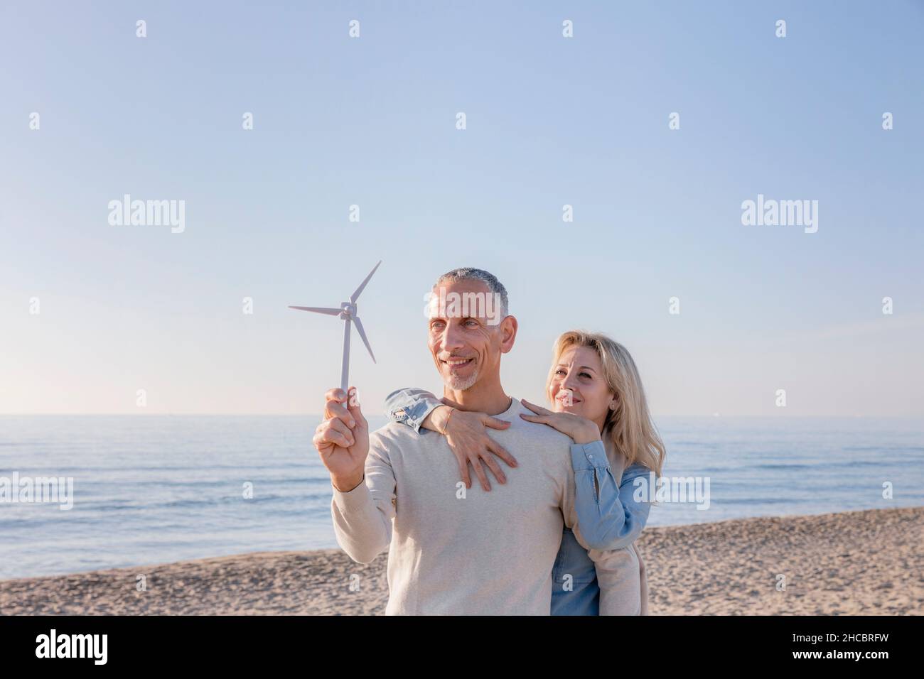 Woman embracing man holding wind turbine model at beach Stock Photo - Alamy