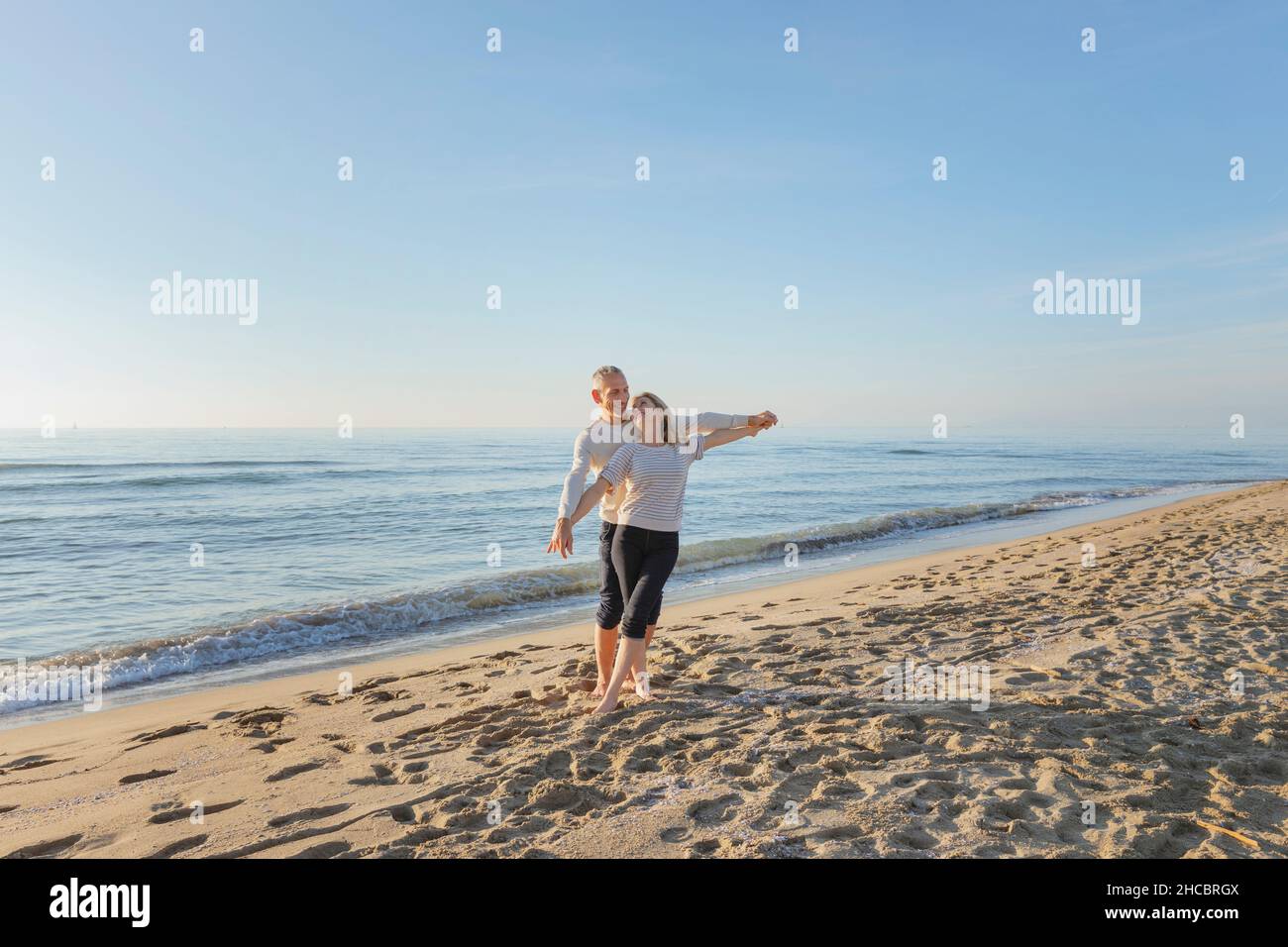 Romantic couple with arms outstretched standing at beach Stock Photo ...