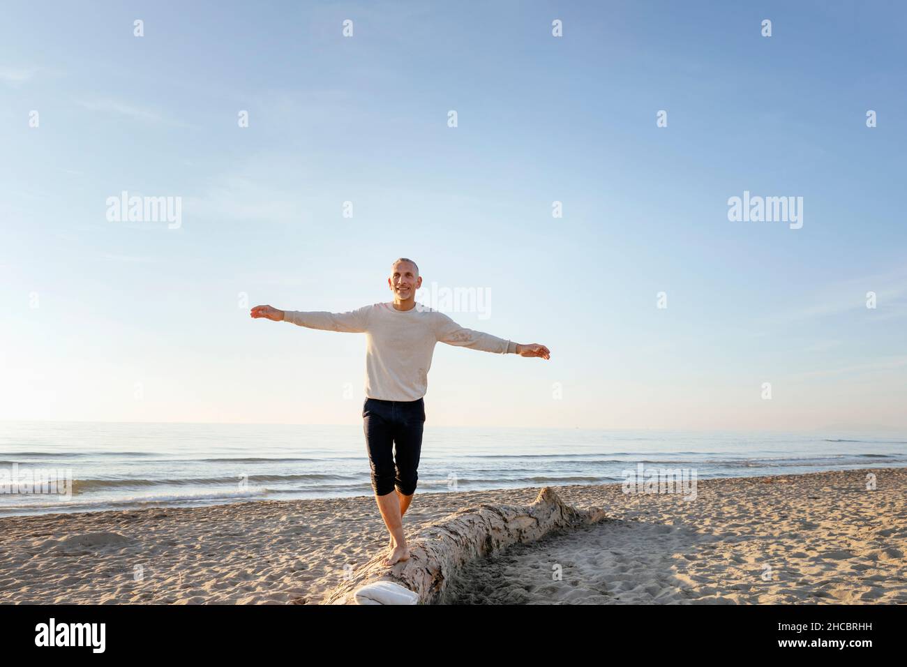 Man balancing on tree log at beach Stock Photo - Alamy