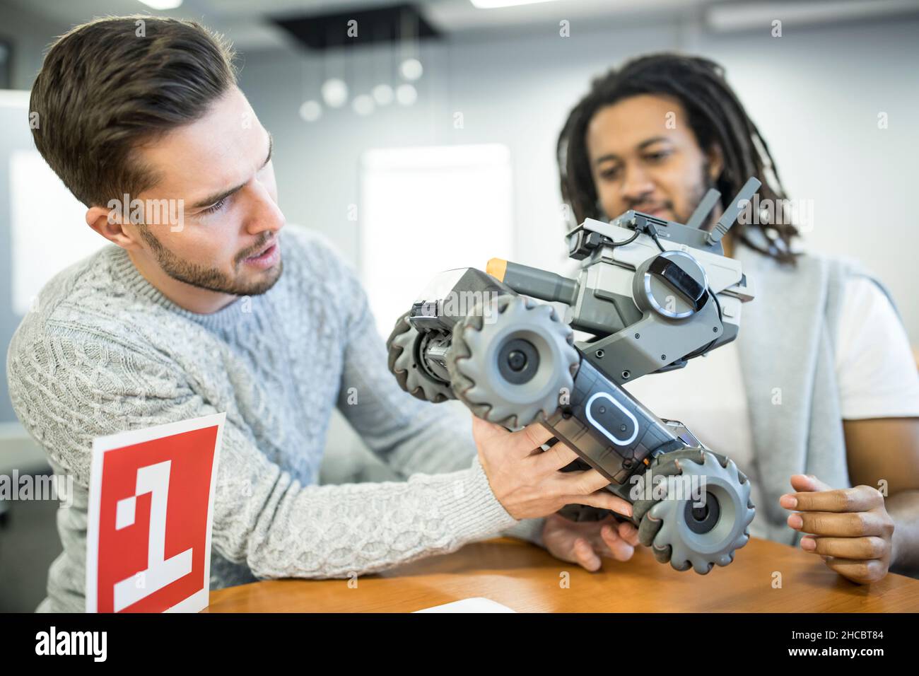 Engineer looking at robotic combat tank with colleague at workshop ...