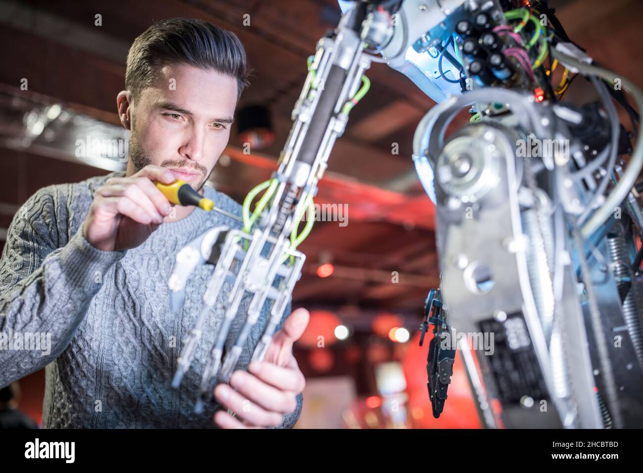 Concentrated engineer fixing robotic arm with screwdriver at workshop ...