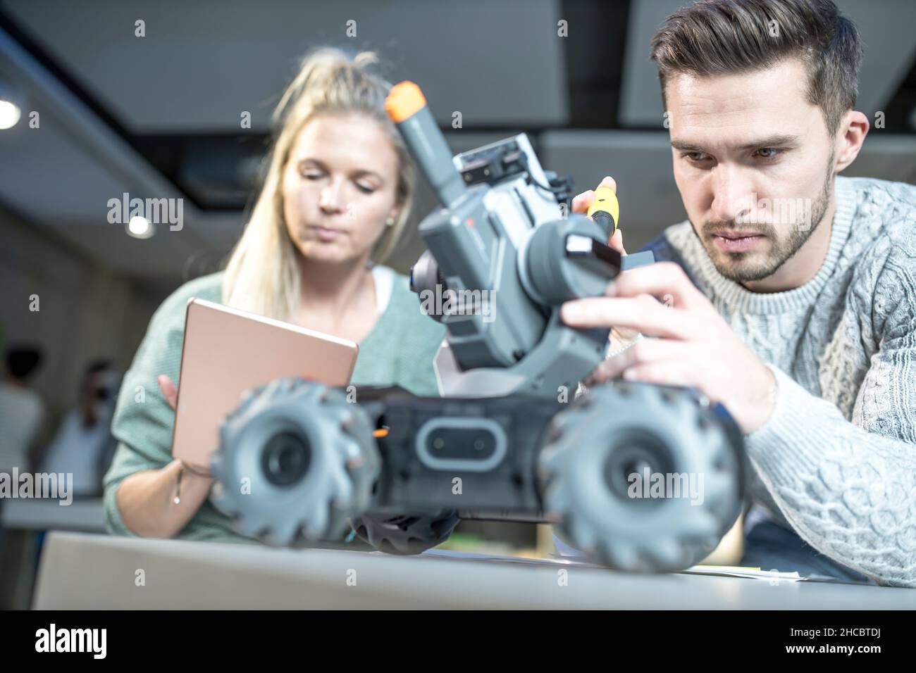 Engineer repairing combat car with colleague programming at workshop ...