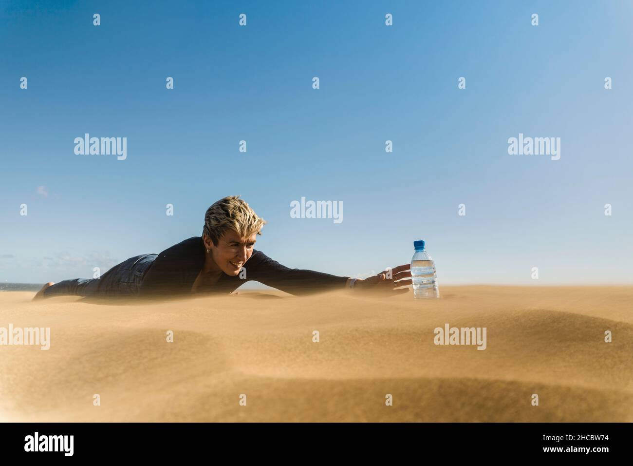 A woman desperately reaching out for bottle of water on the sand desert ...
