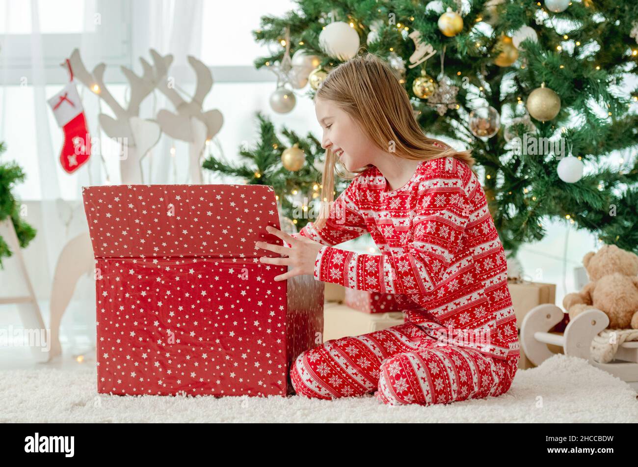 Pretty child girl open Christmas red gift box at home with traditional ...
