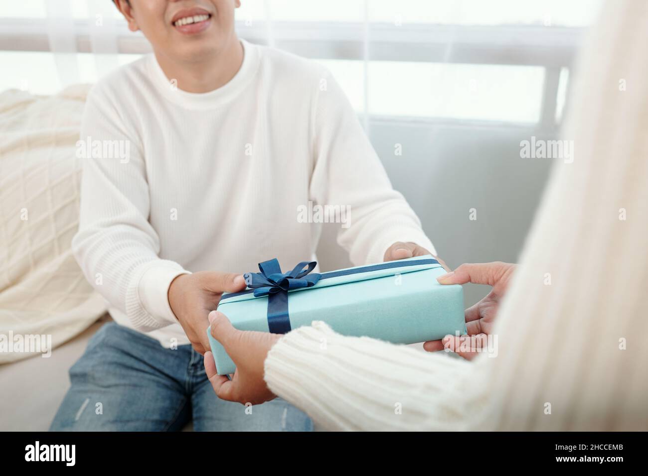 Smiling man accepting Christmas present from his wife wrapped in blue ...