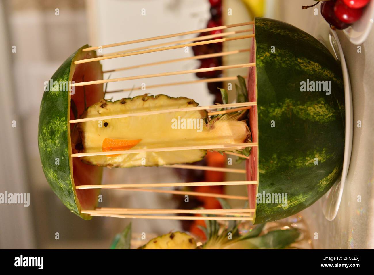 Vertical shot of a parrot made of pineapple inside a watermelon cage ...
