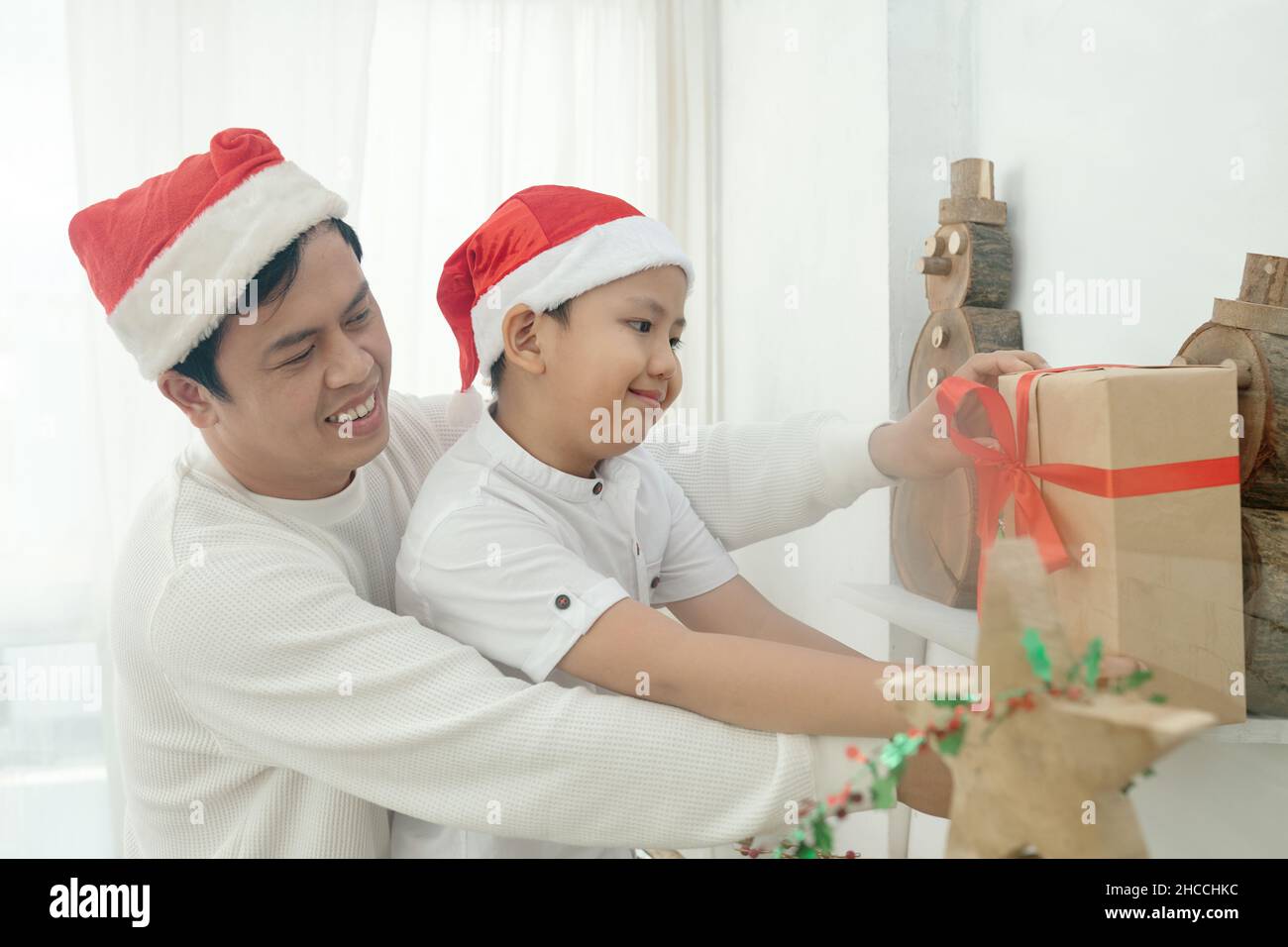Cheerful father helping his son when they are putting wrapped Christmas ...
