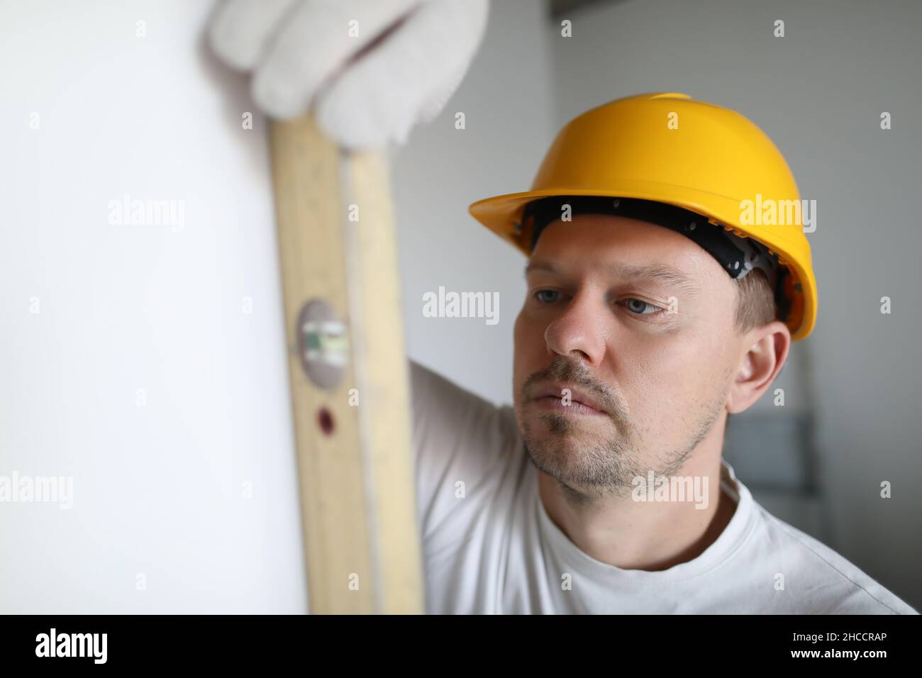 Man in helmet measuring wall using building level in apartment Stock ...