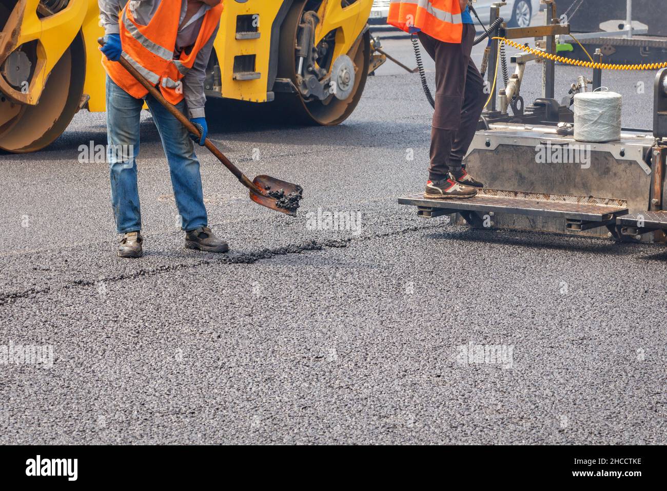 Road workers are repairing a section of road with a shovel, paver and ...