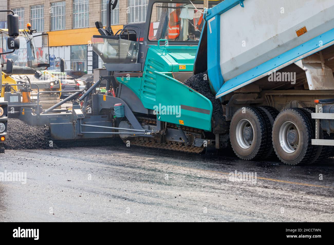 A dump truck unloads asphalt from a body into an asphalt paver at a new ...
