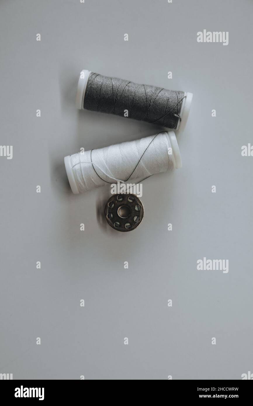 Two spools of white and gray thread and a button lie on a light ...