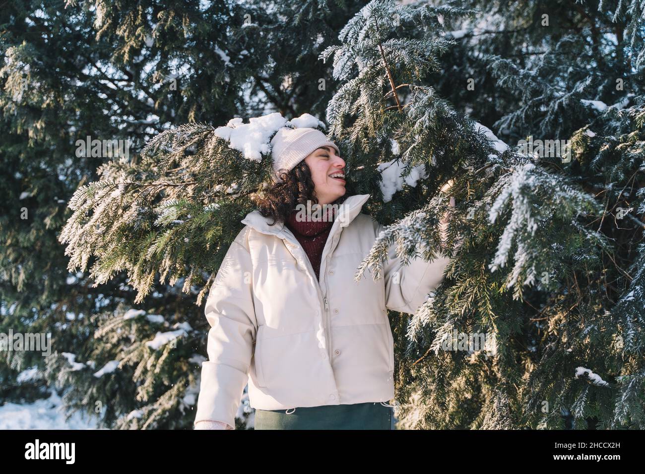 Young curly smiling woman walk in winter park and hide behind snow ...