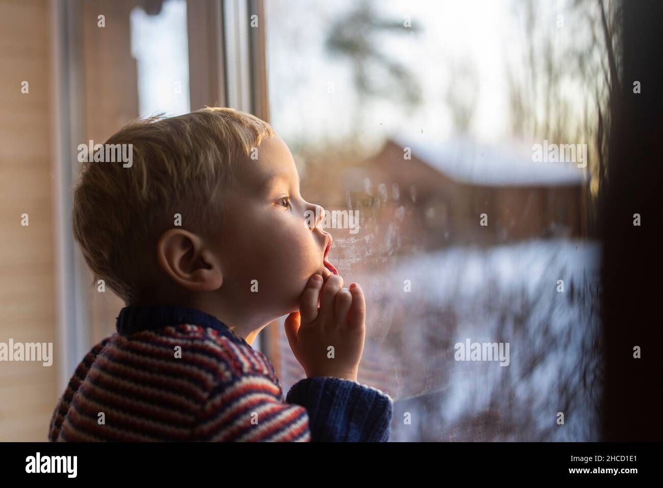 little boy stand near the window and look at the snowy street in winter ...