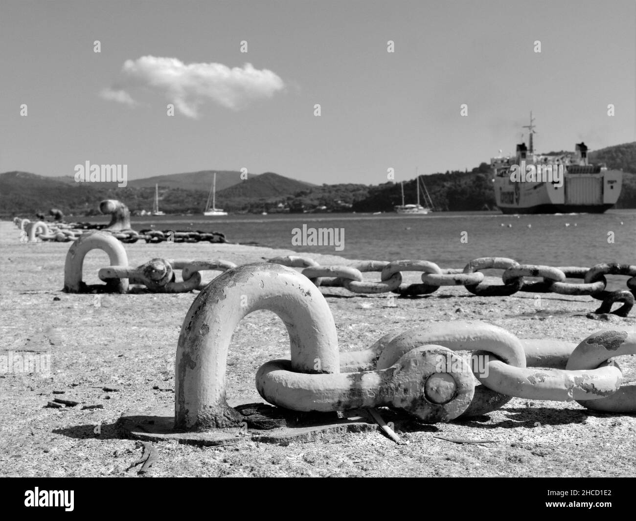 Grayscale closeup of a metal chain on a pavement anchor near water with ...