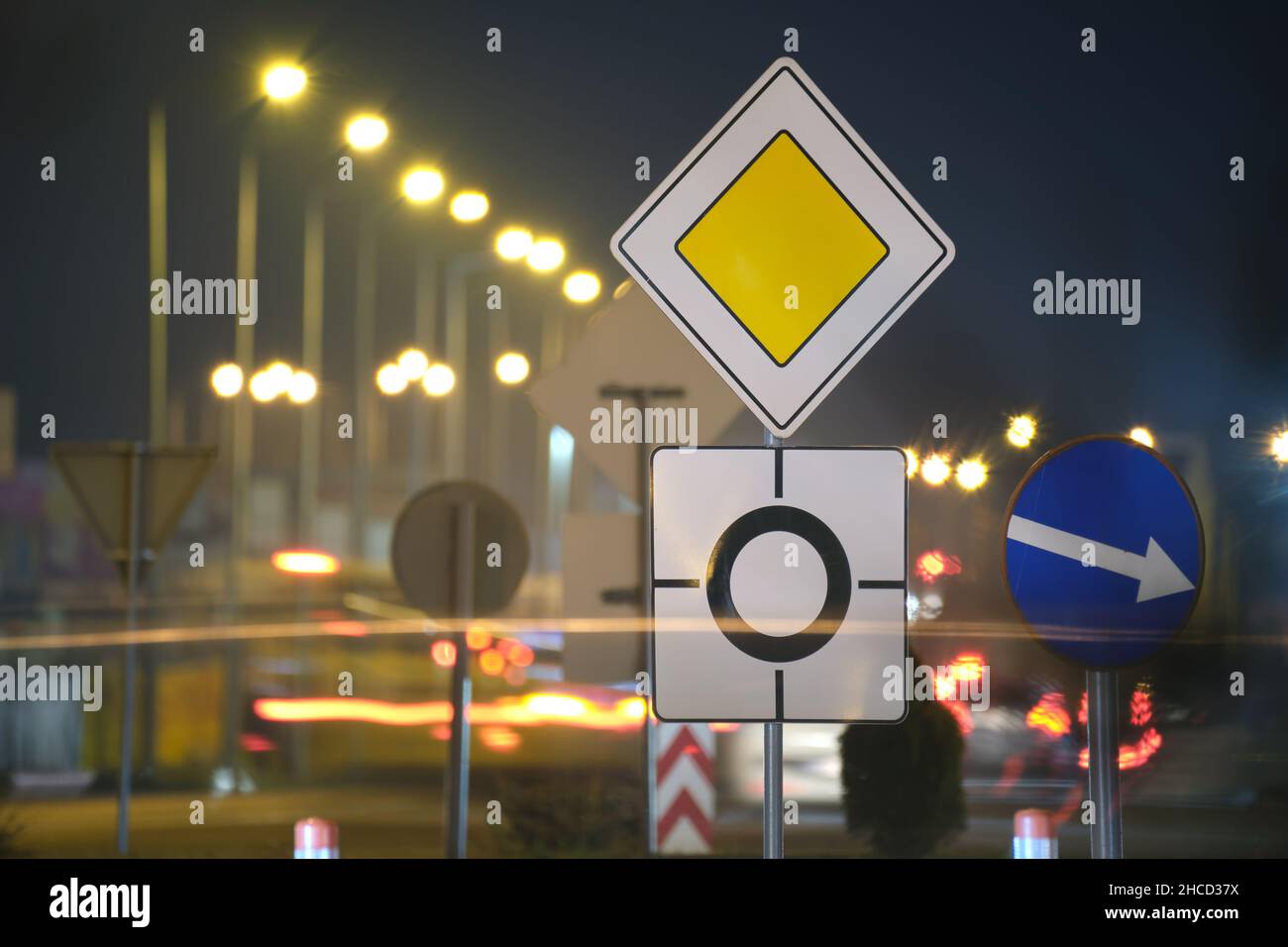 Roundabout road signs with blurred cars on city street traffic at night ...