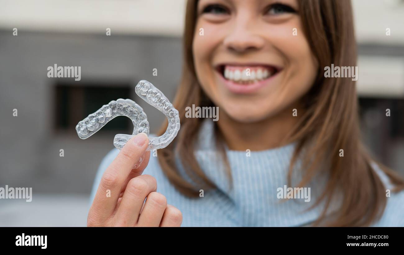 Caucasian woman with white smile holding transparent removable retainer ...