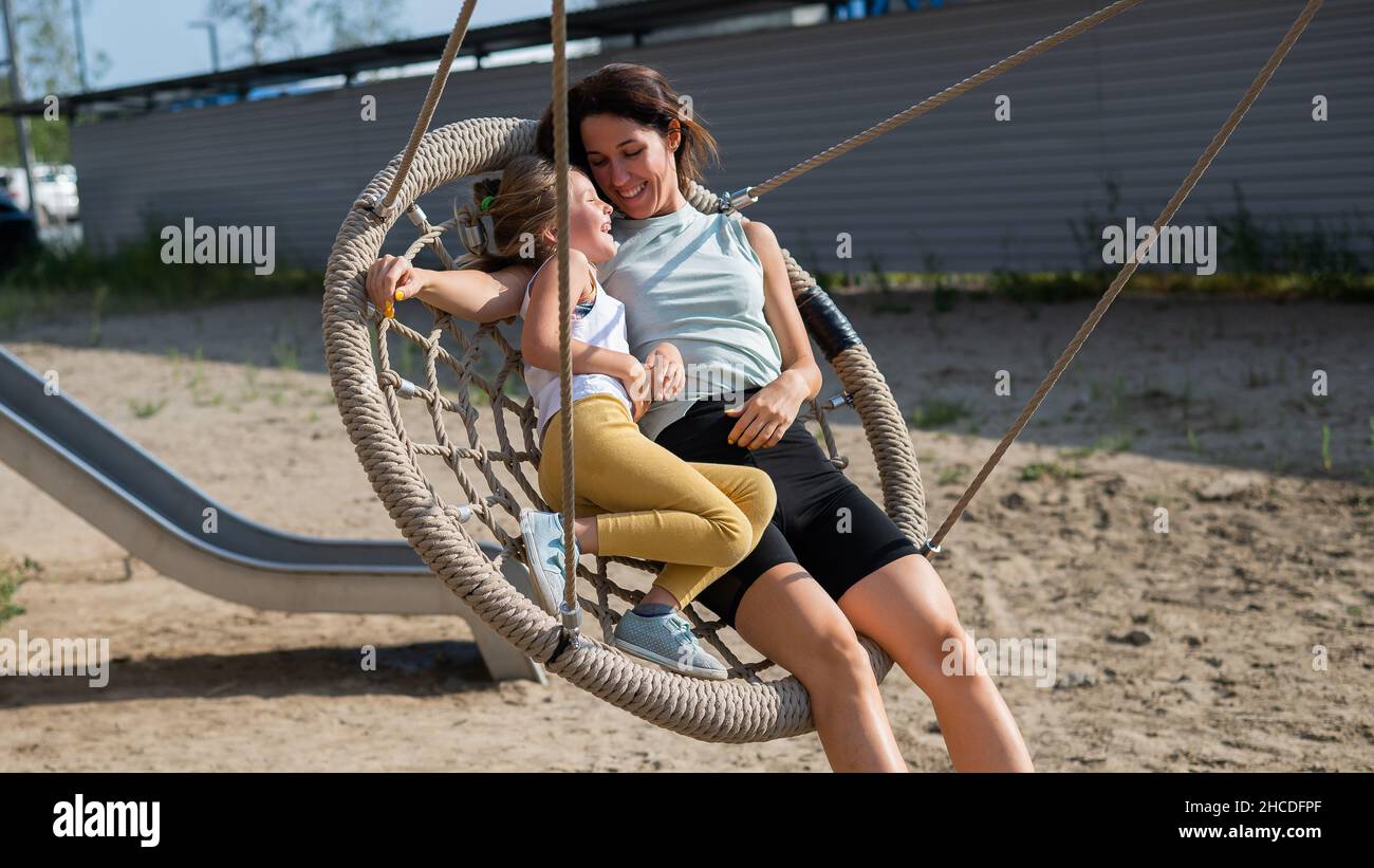 Mom and daughter swing on a round swing. Caucasian woman and little girl have fun on the ...