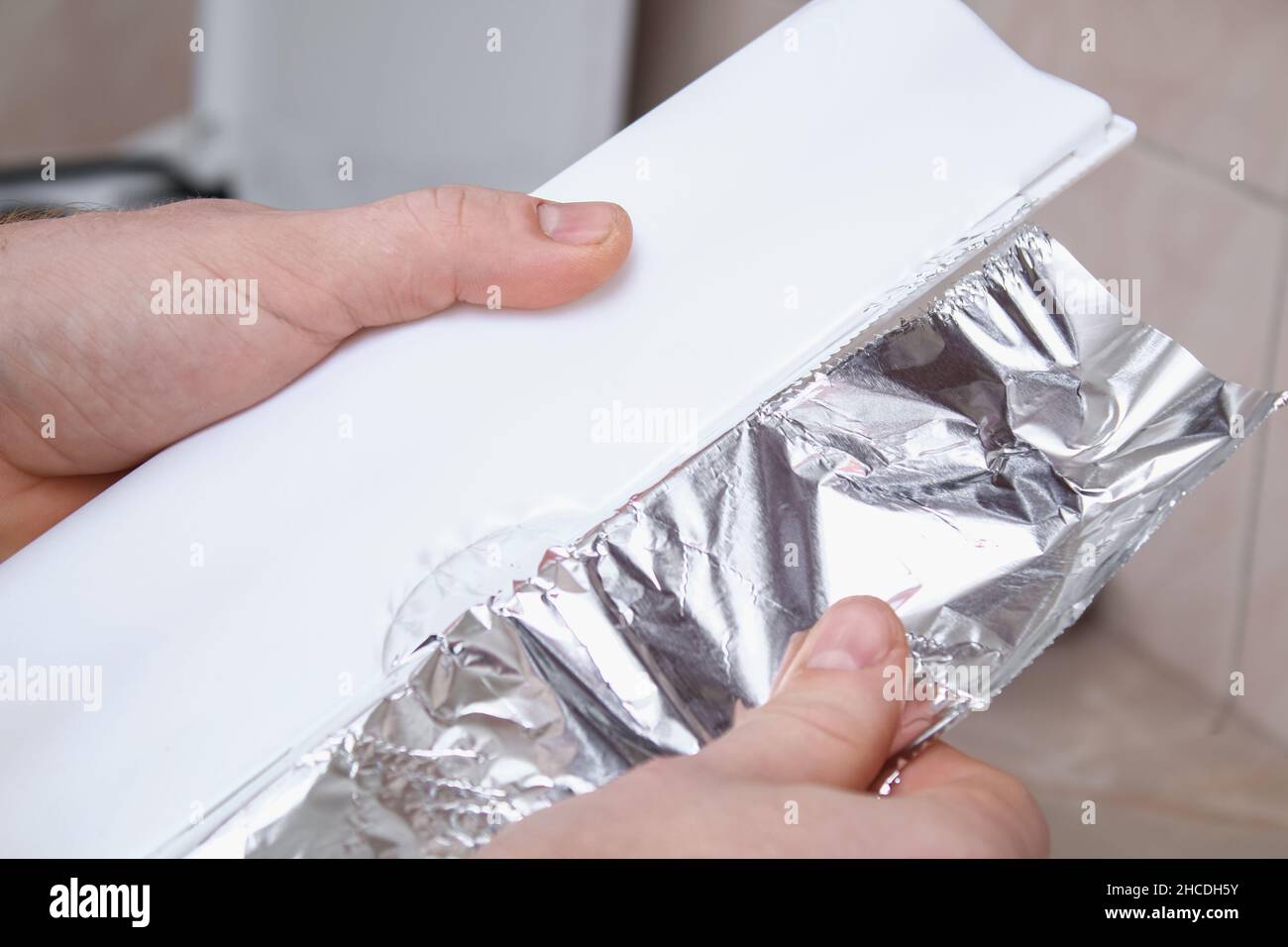 A man tears off the foil from a plastic dispenser to wrap potatoes in ...