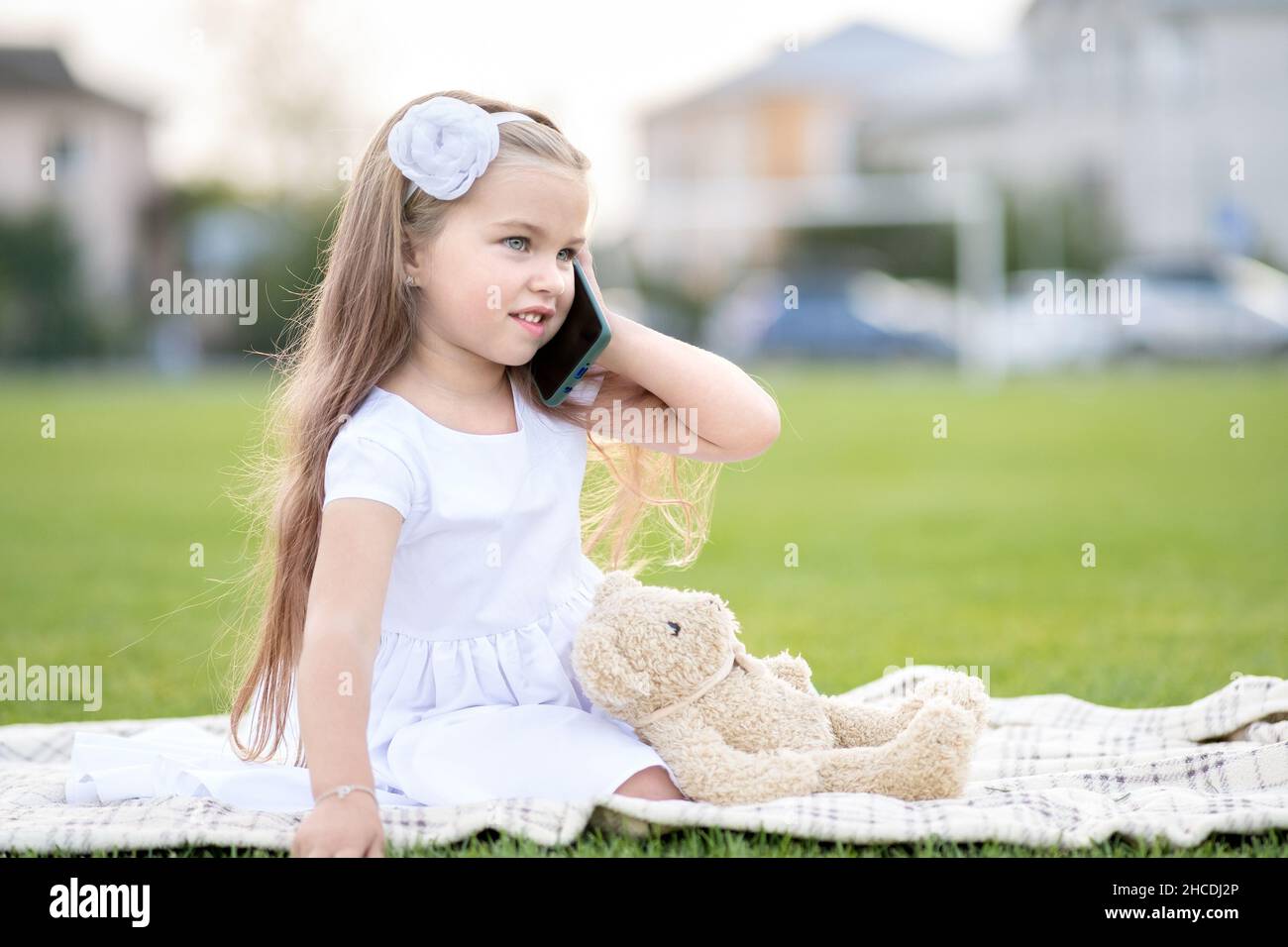 Pretty little child girl sitting in summer park together with her teddy ...