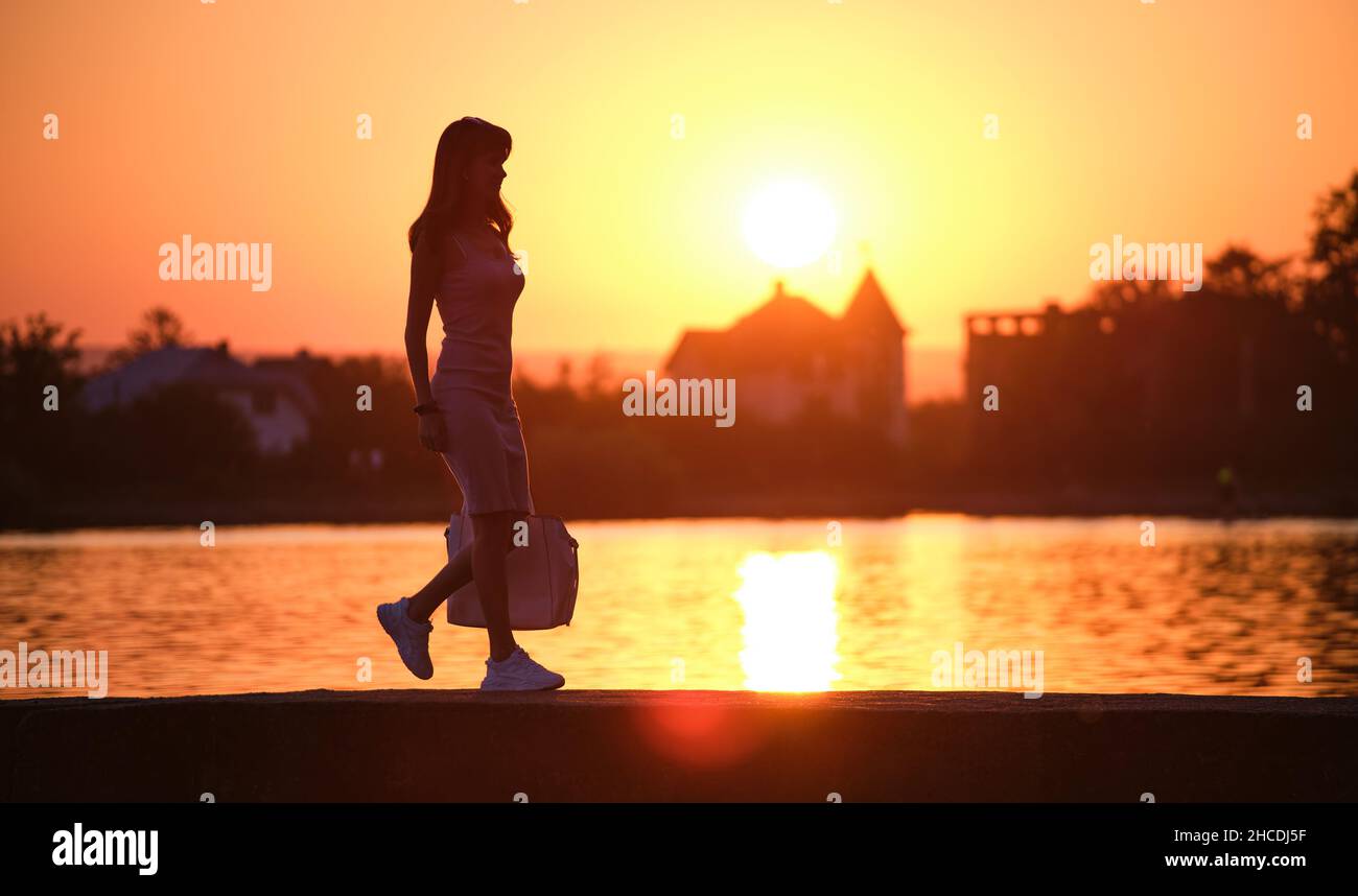 Young woman walking alone on lake shore walkway on warm evening ...