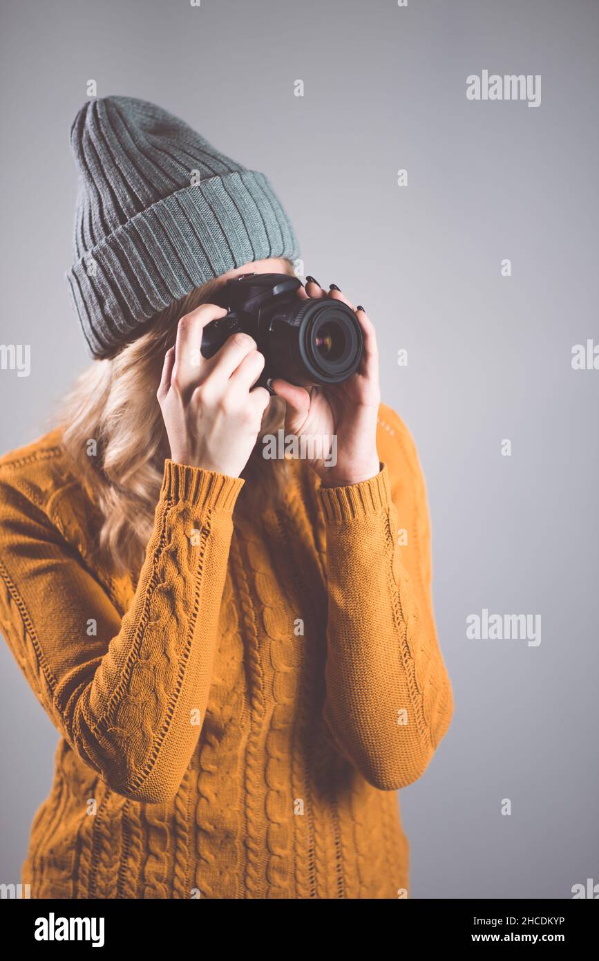A beautiful woman photographer in a knitted hat is photographed with a ...
