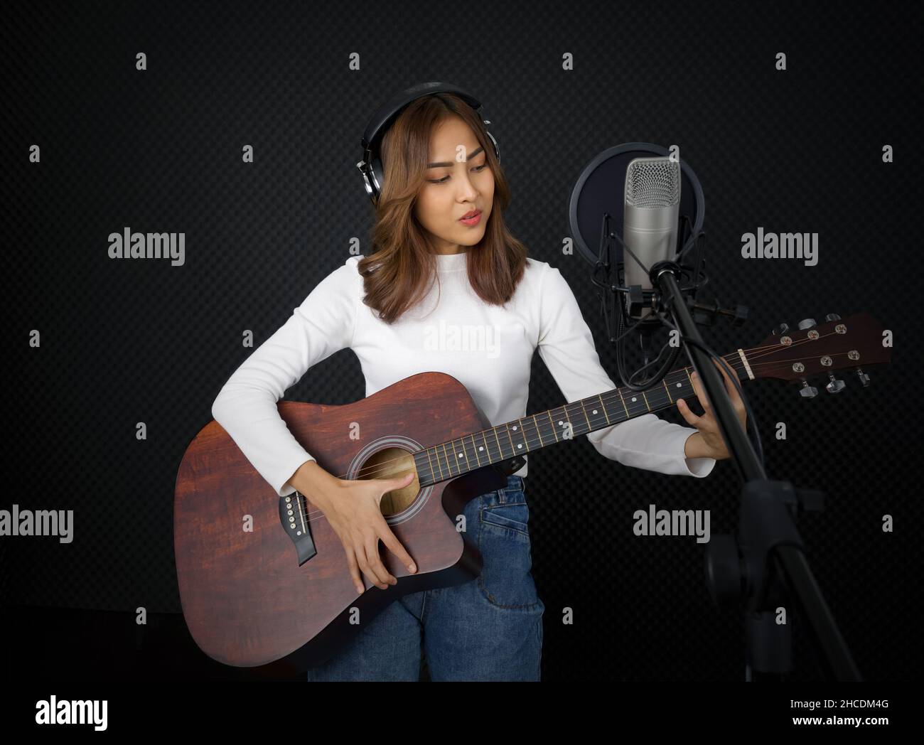 Young asian woman with headphone sing while playing an acoustic guitar ...