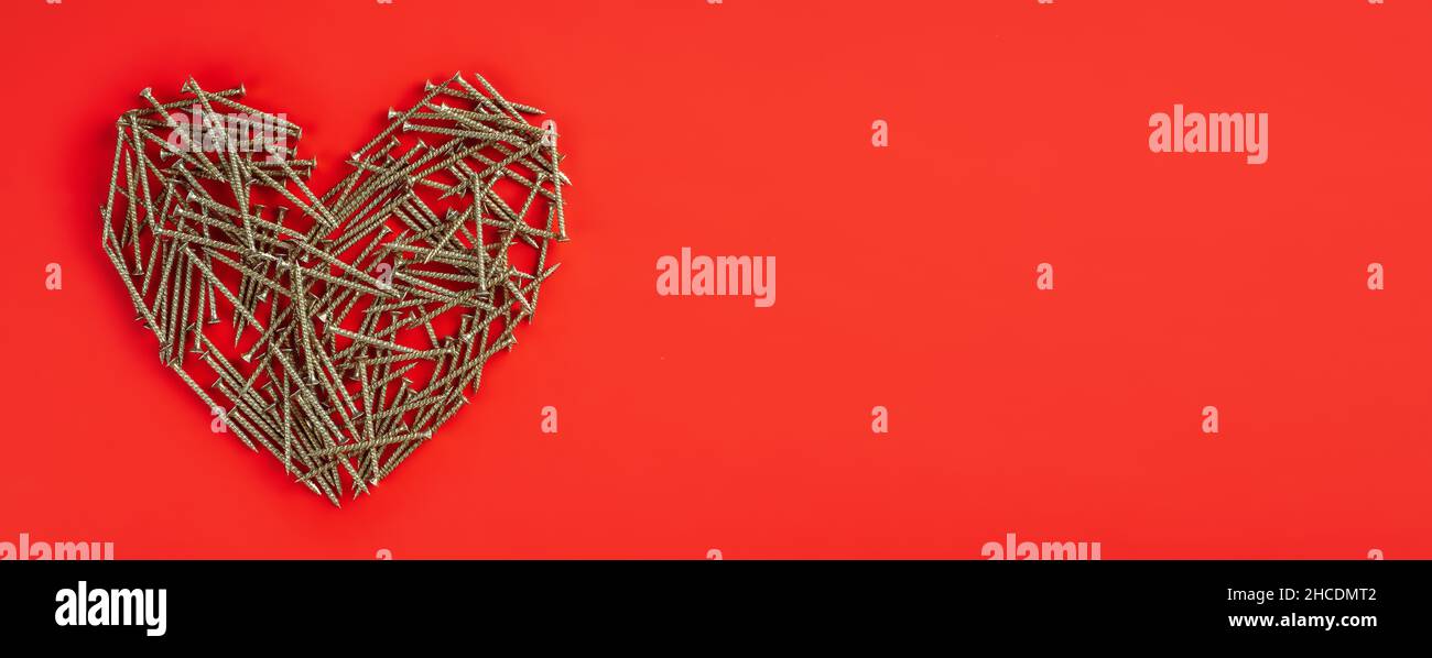 Small metal nails laid out randomly in shape of heart on red background ...