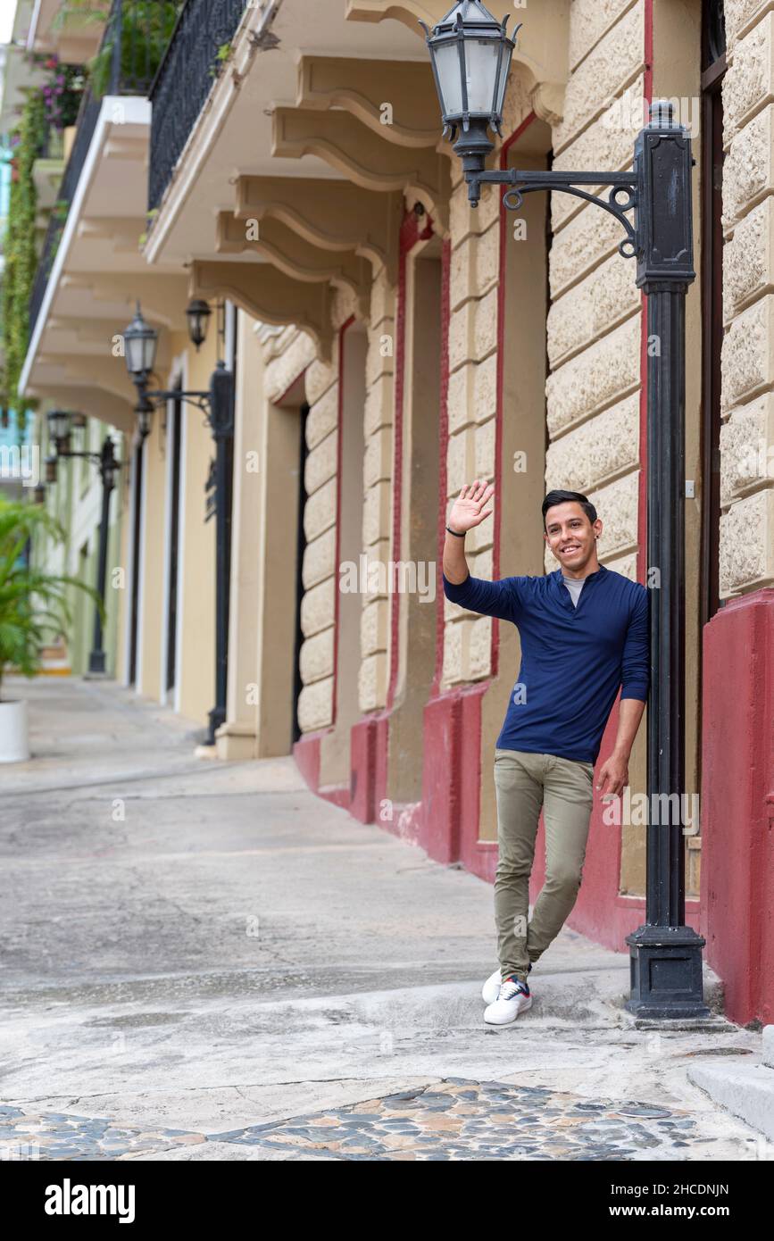 A portrait of a stylish young man waving standing on a city street ...