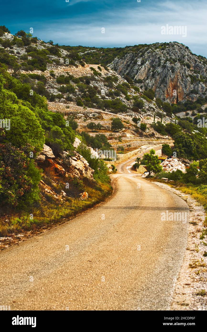 Narrow road leading to a stony mountainous valley with green trees and ...