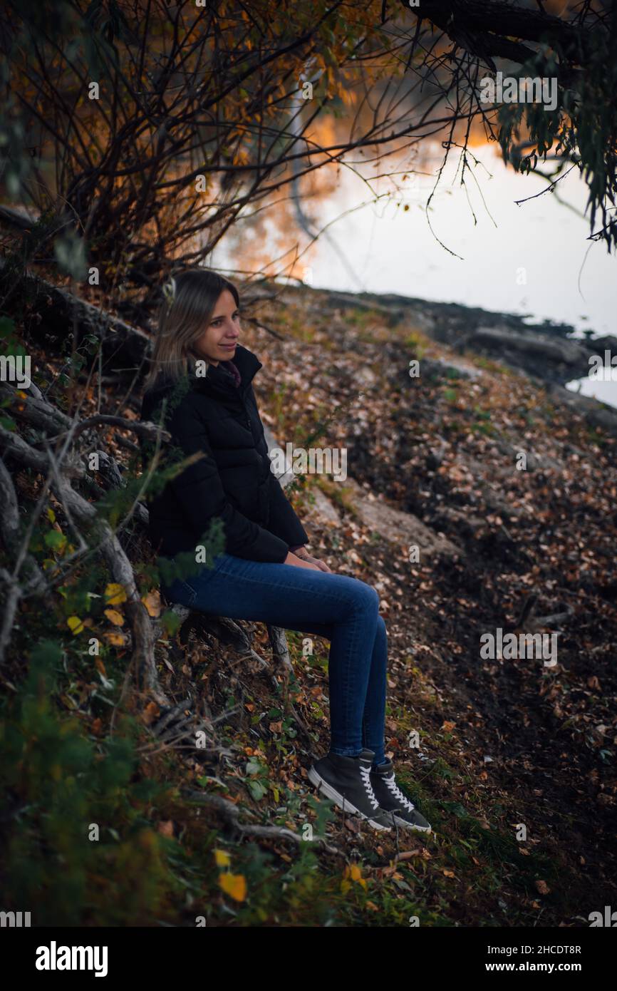 Shining young woman sitting on tree roots in forest, smiling, looking ...