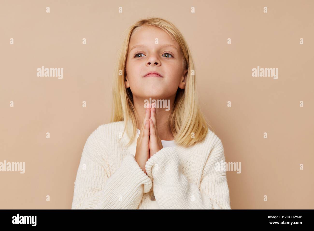 Portrait of a smiling little cutie in a sweater, grimaces on a beige ...