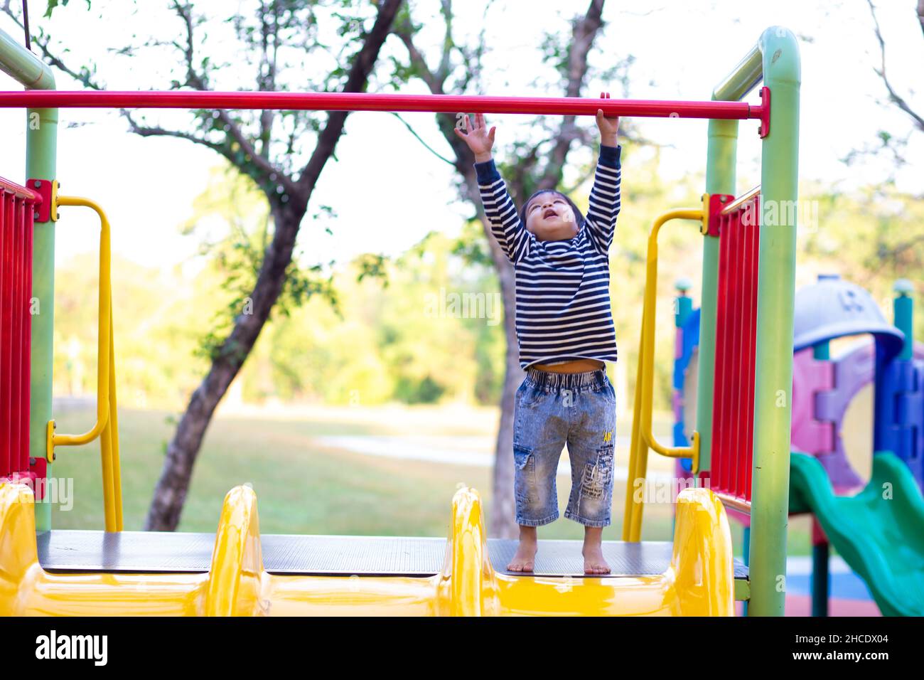 Asian preschool boy climbing on playground climb bar in city public ...