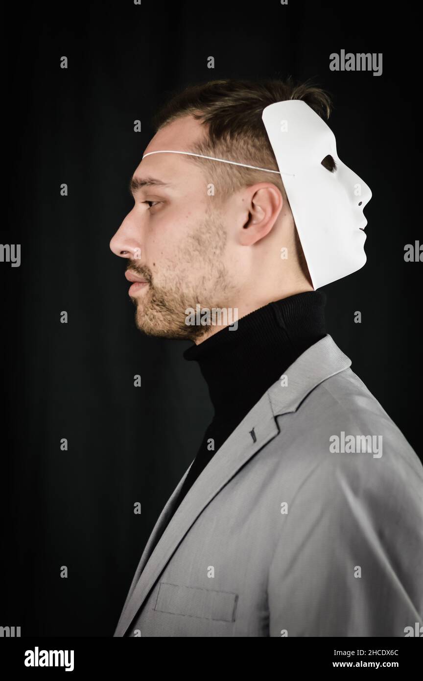 Dual personality - young man holding a white mask behind his neck ...