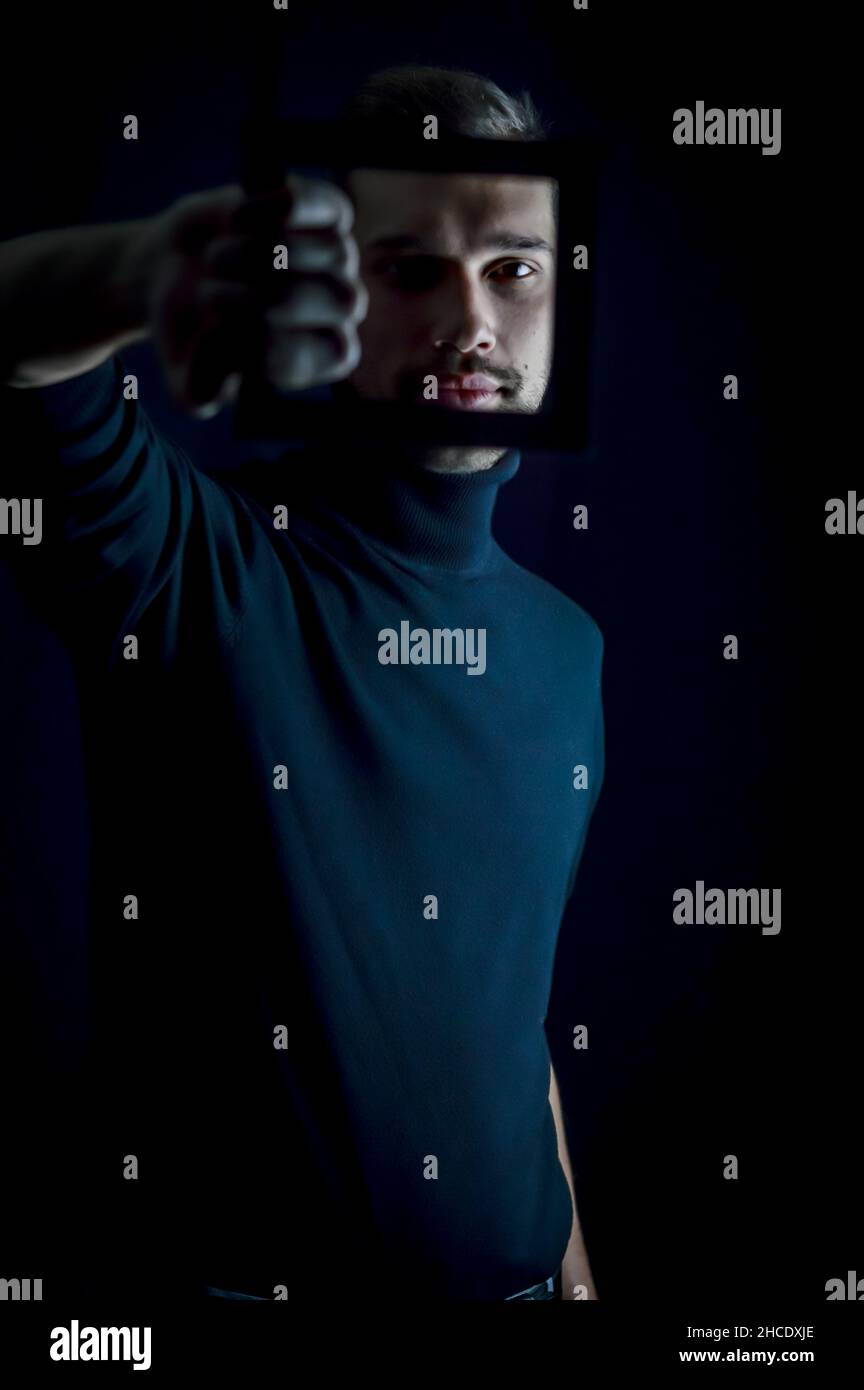 portrait of a young man holding a frame in front of his face, concept ...