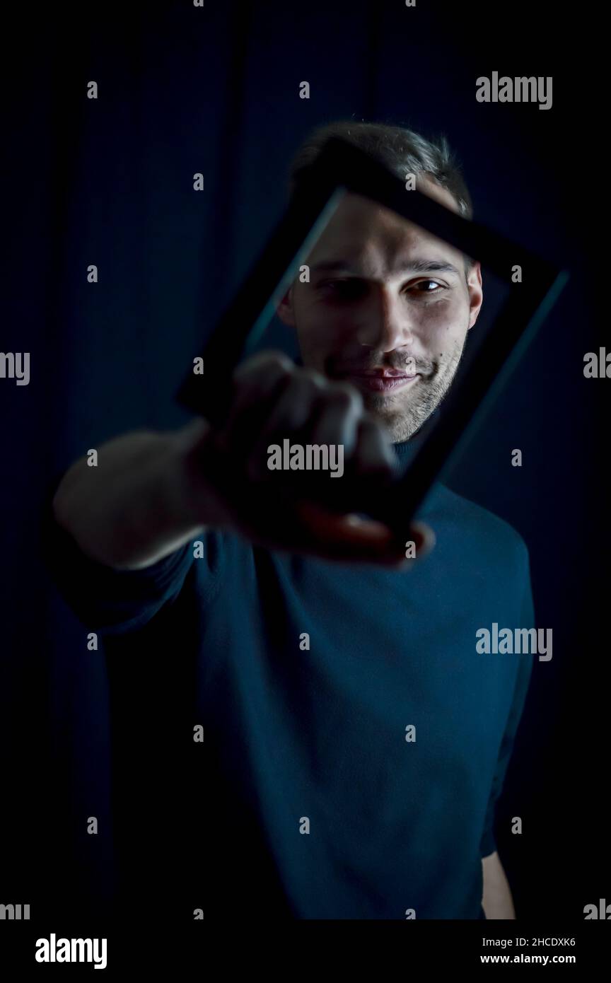 portrait of a young man holding a frame in front of his face, concept ...