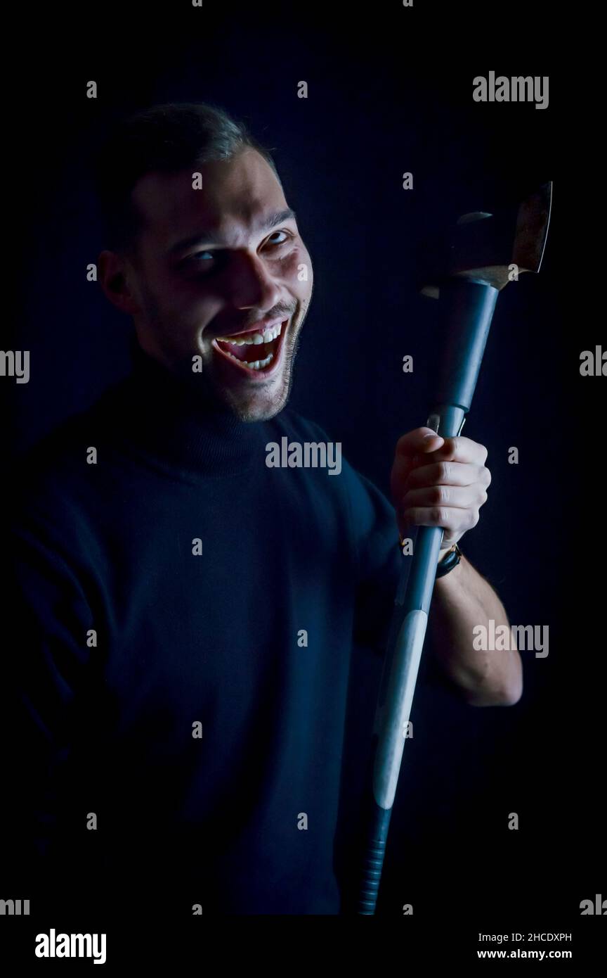 portrait of a scary young man laughing evil with an ax in his hand ...
