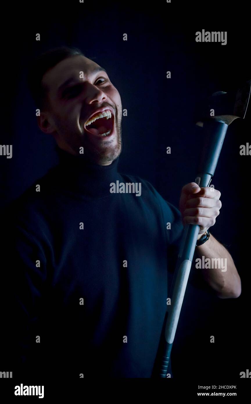 portrait of a scary young man laughing evil with an ax in his hand ...