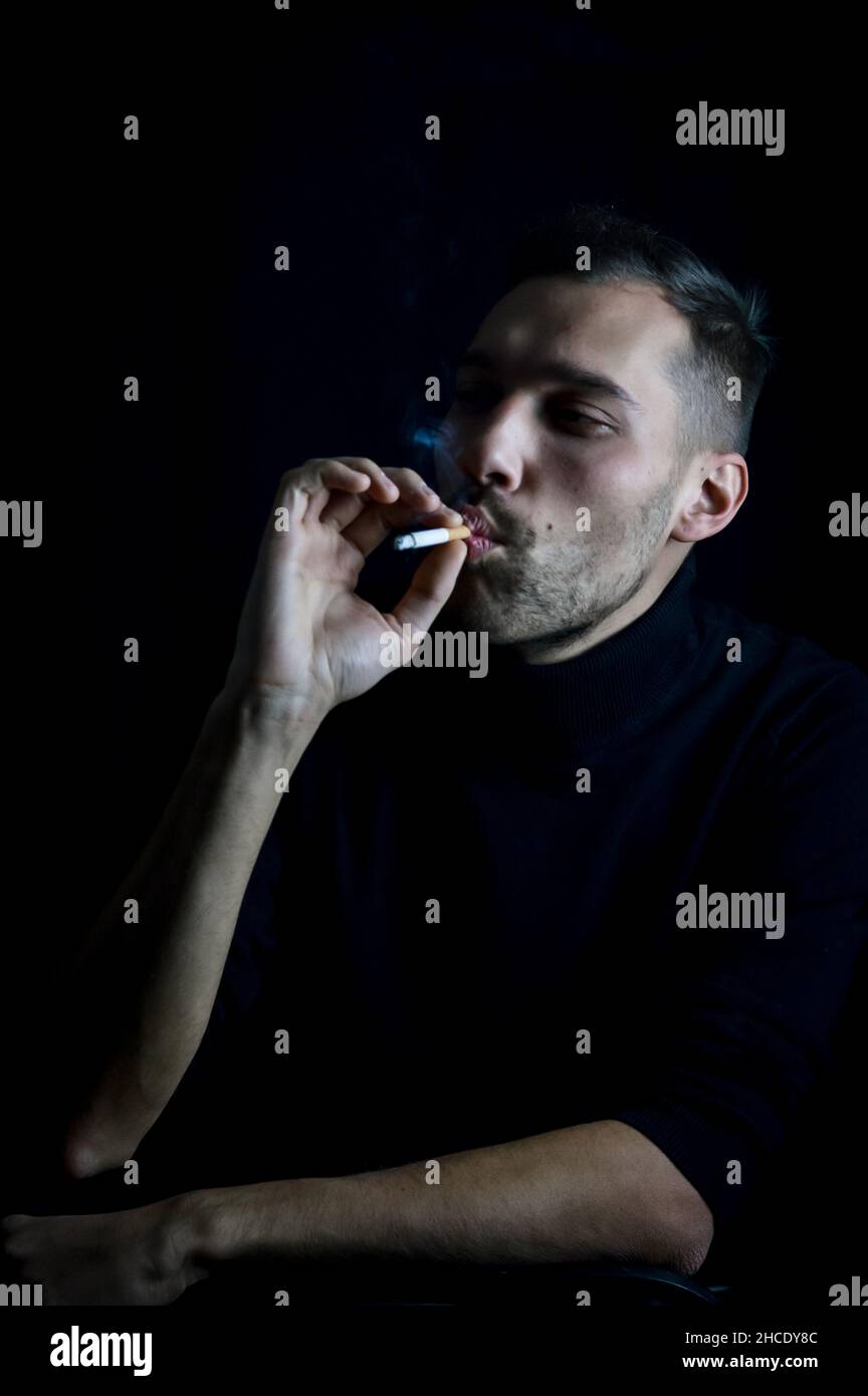 portrait of a young man who is inhaling the smoke of a cigarette while ...