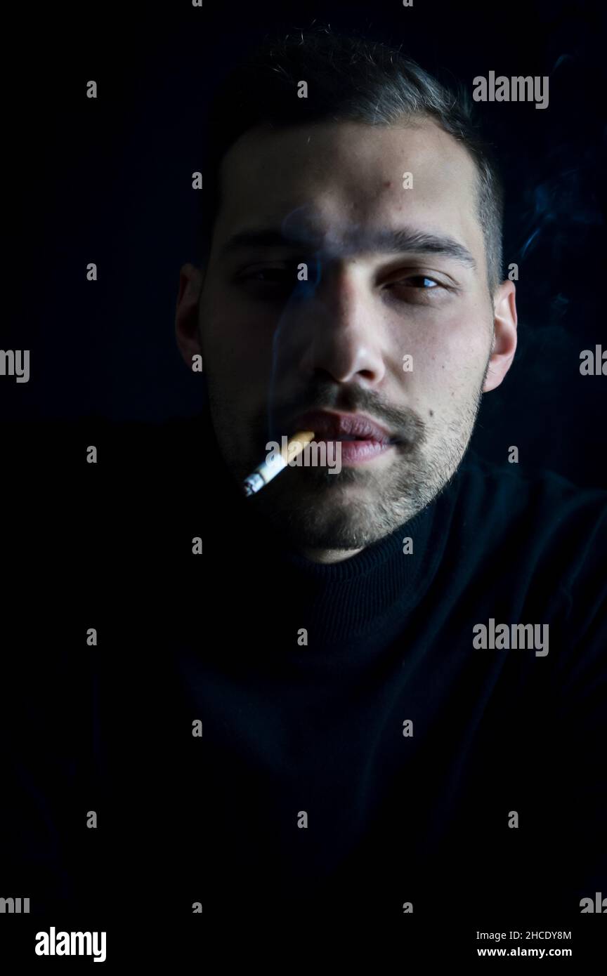 portrait of a young man holding a lit cigarette between his lips with ...