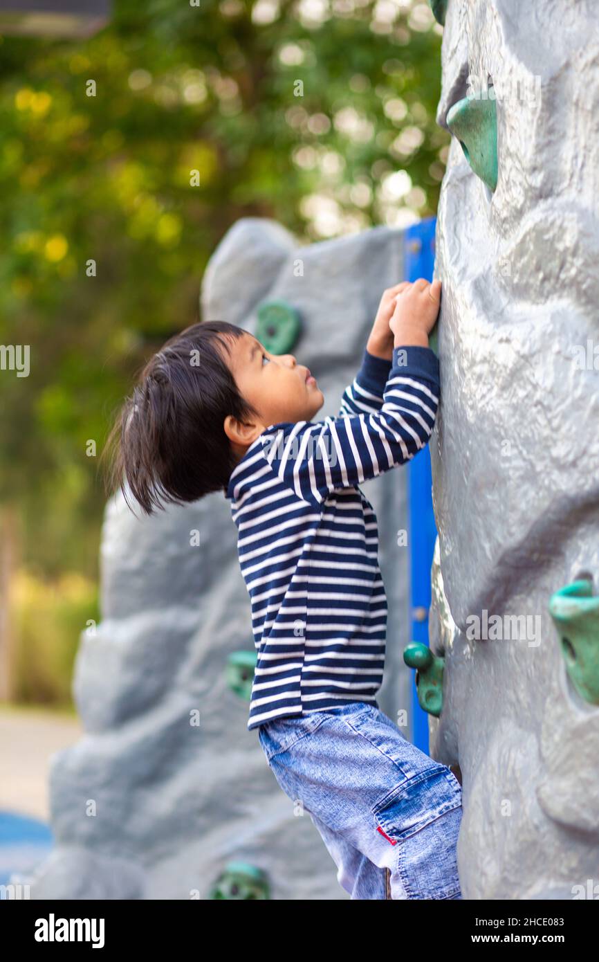 Asian preschool boy climbing on playground climb bar in city public ...
