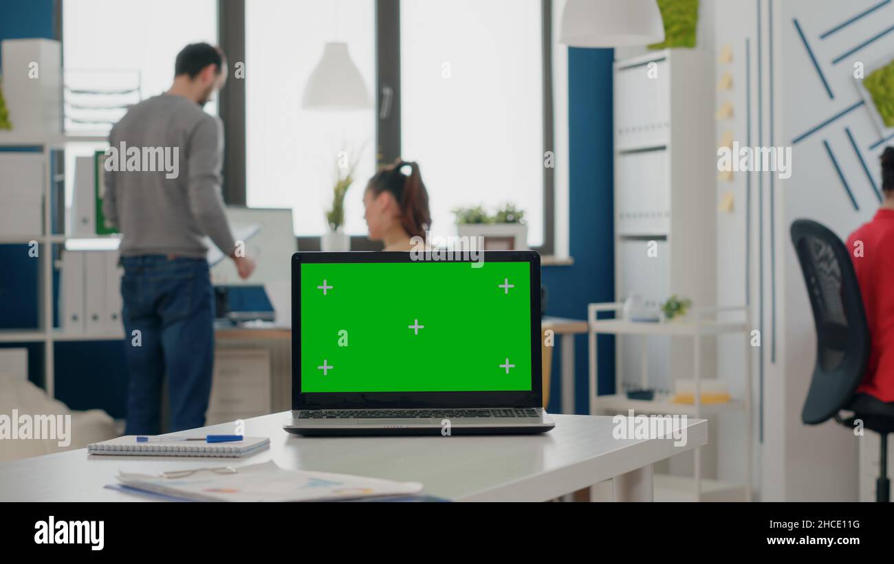 Close up of empty desk with green screen on laptop in startup office ...