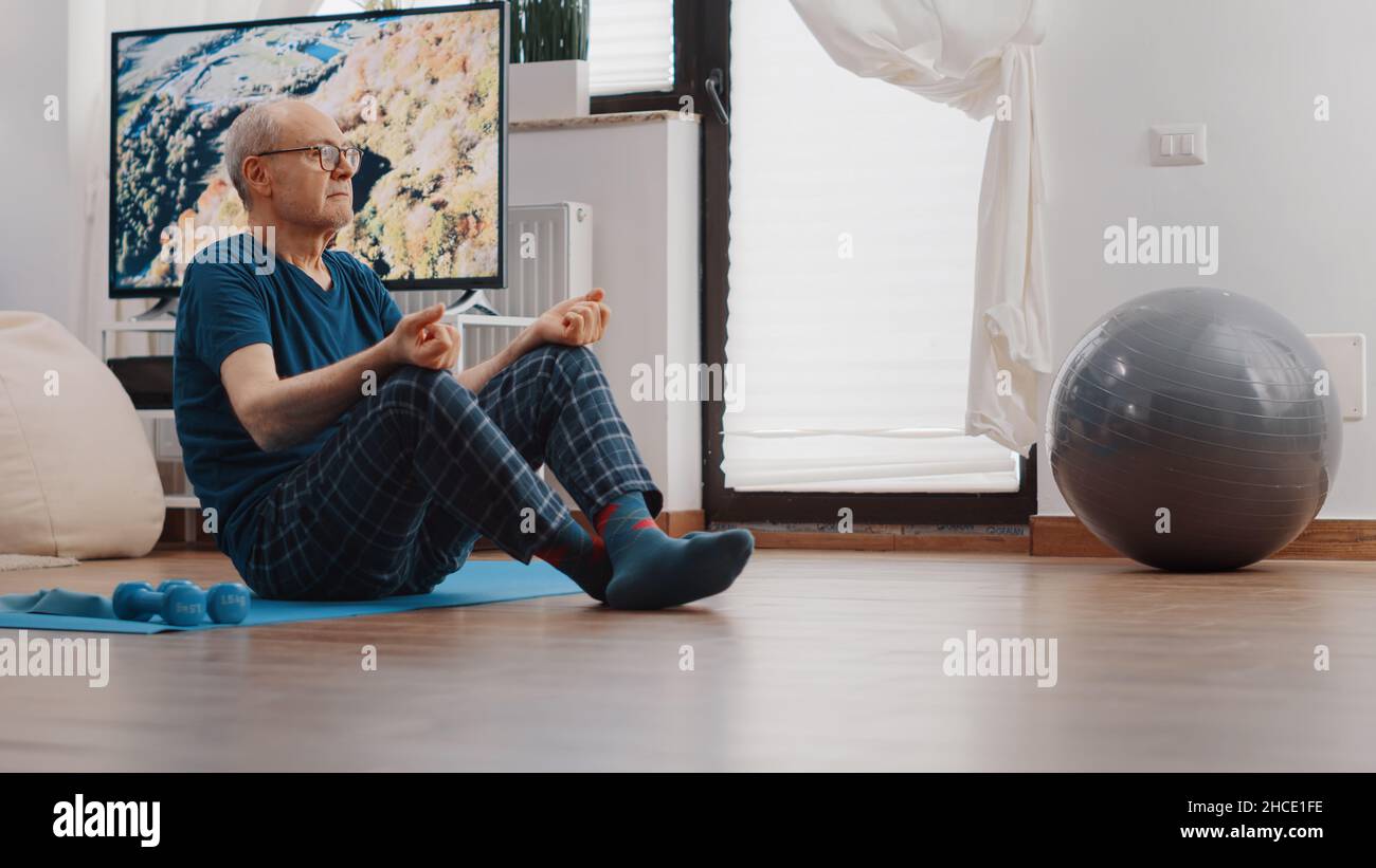 Senior man sitting in lotus position and doing meditation on yoga mat ...