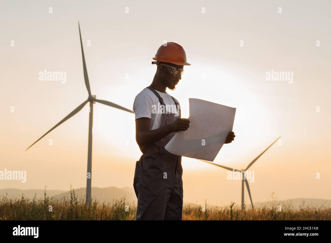 Focused african american man with blueprints in hands standing among ...