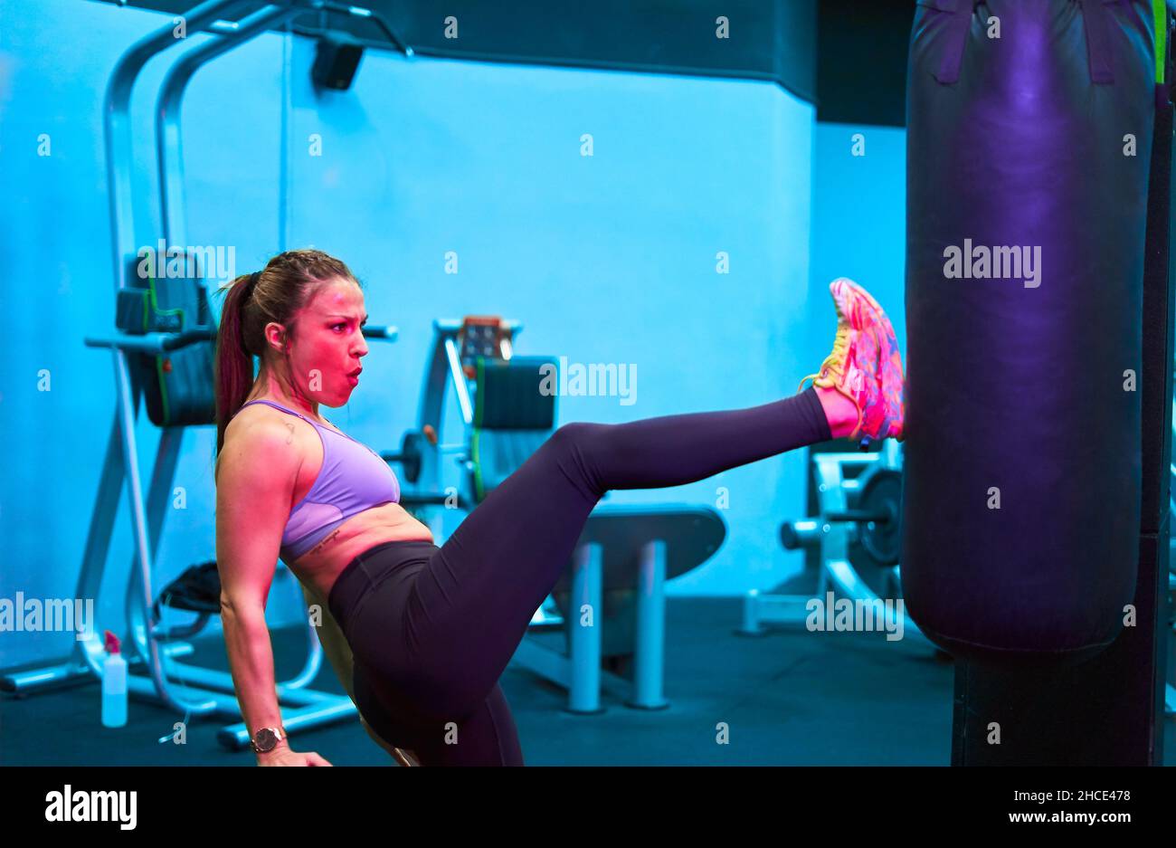 Side view of athletic Hispanic Woman kicking boxing bag while training ...