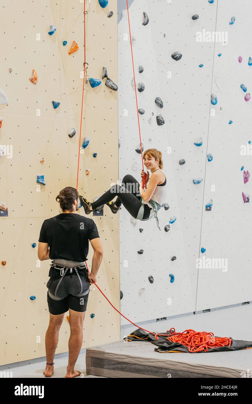 Back view man in activewear helping female alpinist to climb artificial ...