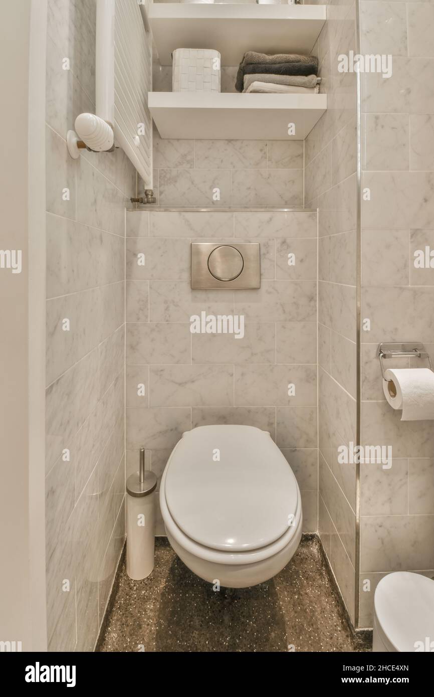 White ceramic toilet placed at tiled wall in light lavatory room with ...