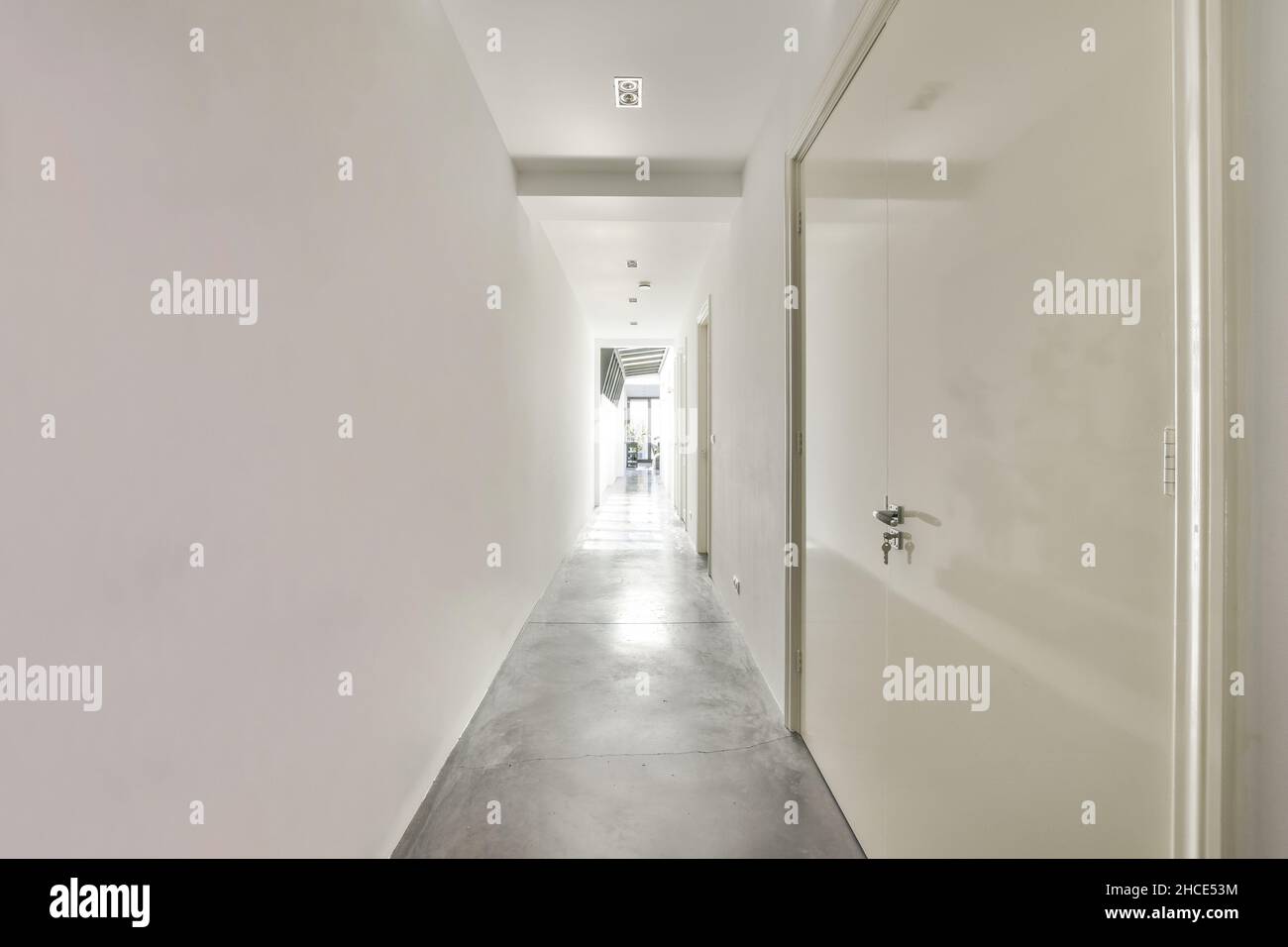 Long narrow corridor with clear white walls and closed room doors ...