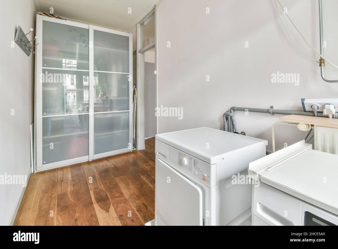 White washing machine placed on wooden floor in corner near wall ...