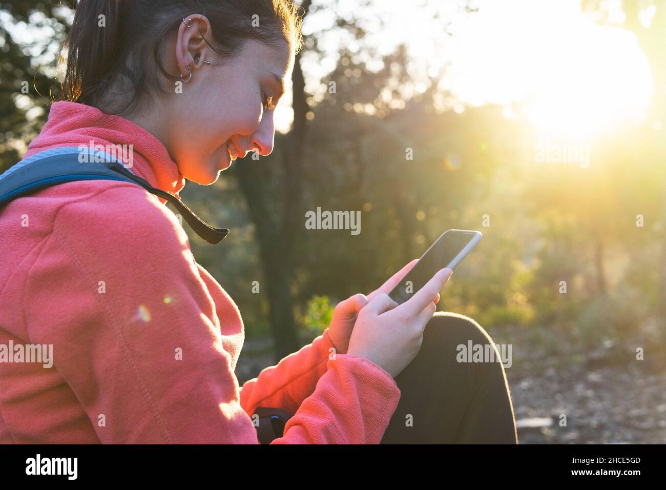 Side view of smiling female hiker text messaging on modern cellphone ...